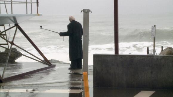 'Oceanside trenchcoat guy' takes on rain and waves as storm hits North ...
